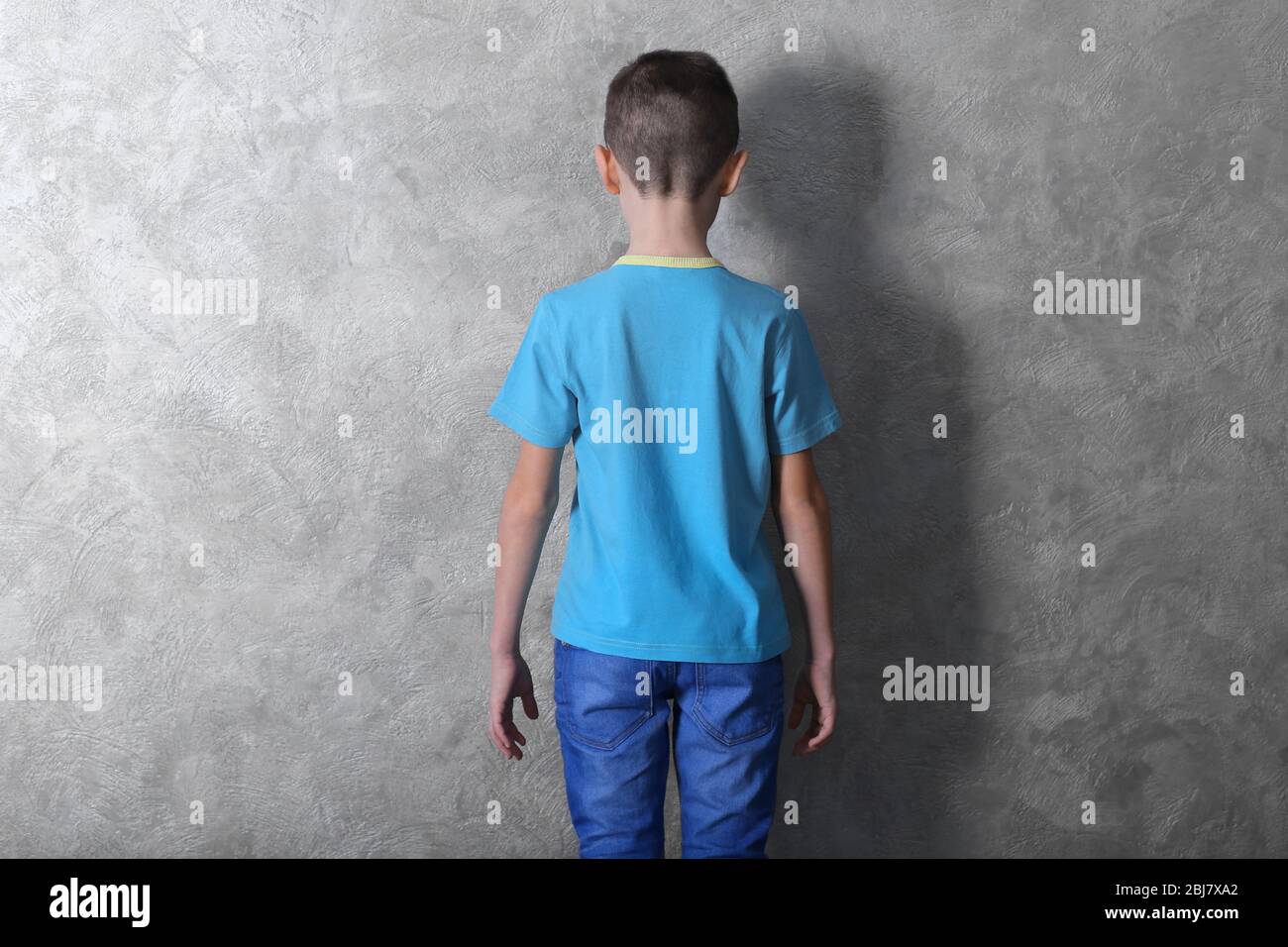 Clothes advertising. Boy in blue T-shirt and jeans against grey ...