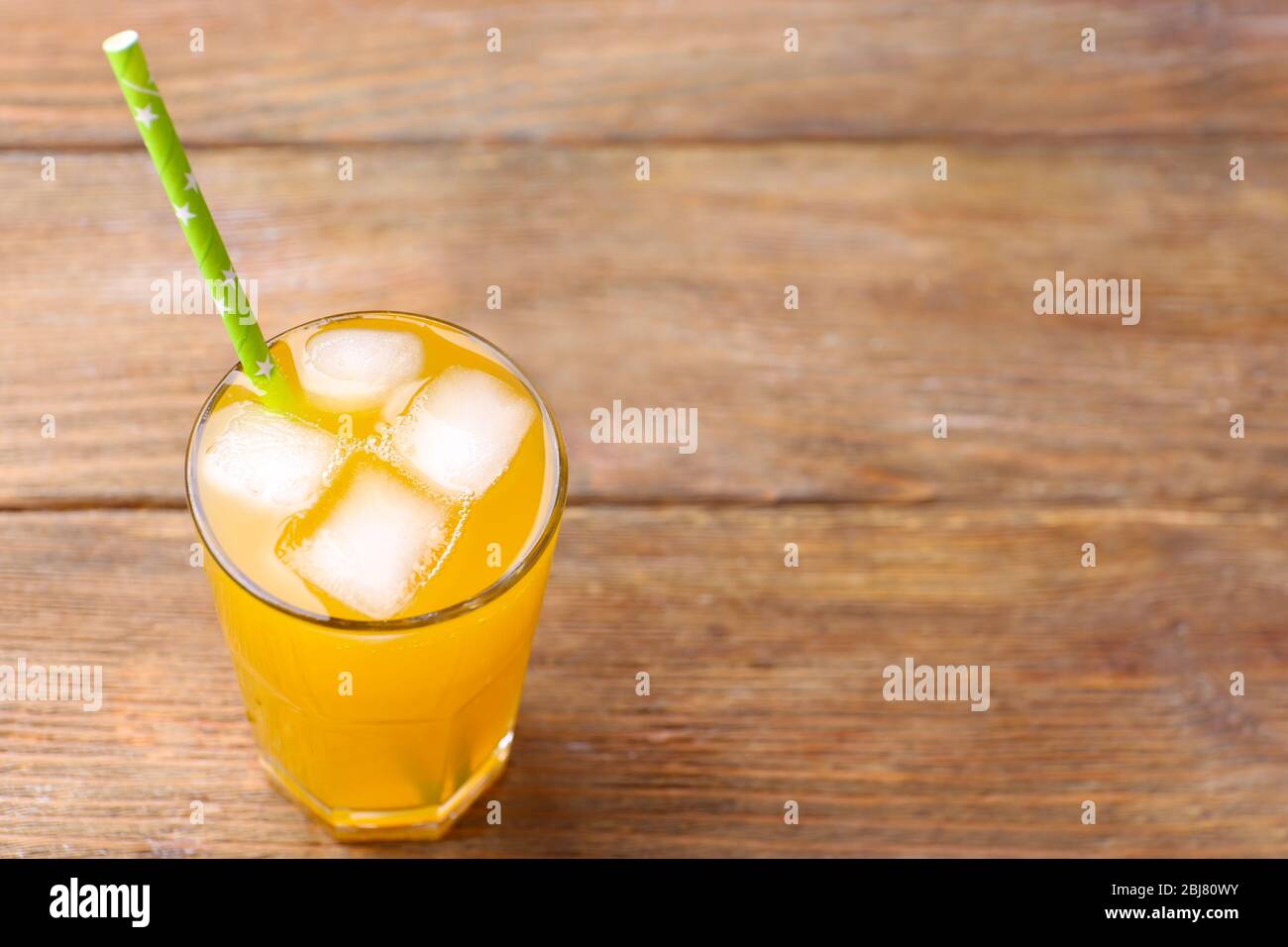 Glass of orange juice with ice blocks and tubule on wooden background ...
