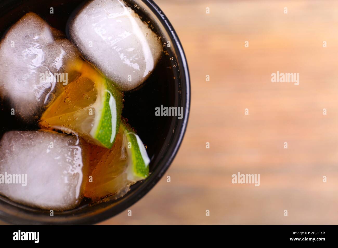 Cocktail with lime slices and ice blocks on wooden table, close up ...
