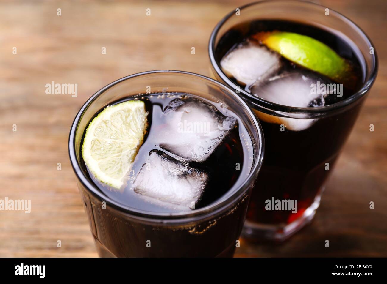 Cocktails with lime slices and ice blocks on wooden table, close up ...