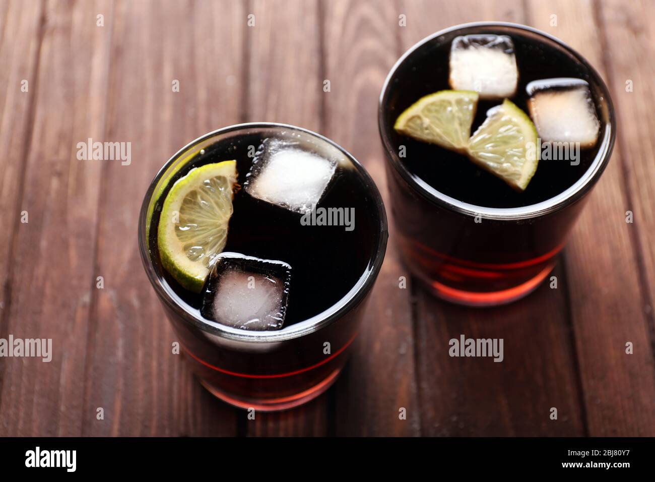 Cocktails with lime slices and ice blocks on wooden table, close up ...
