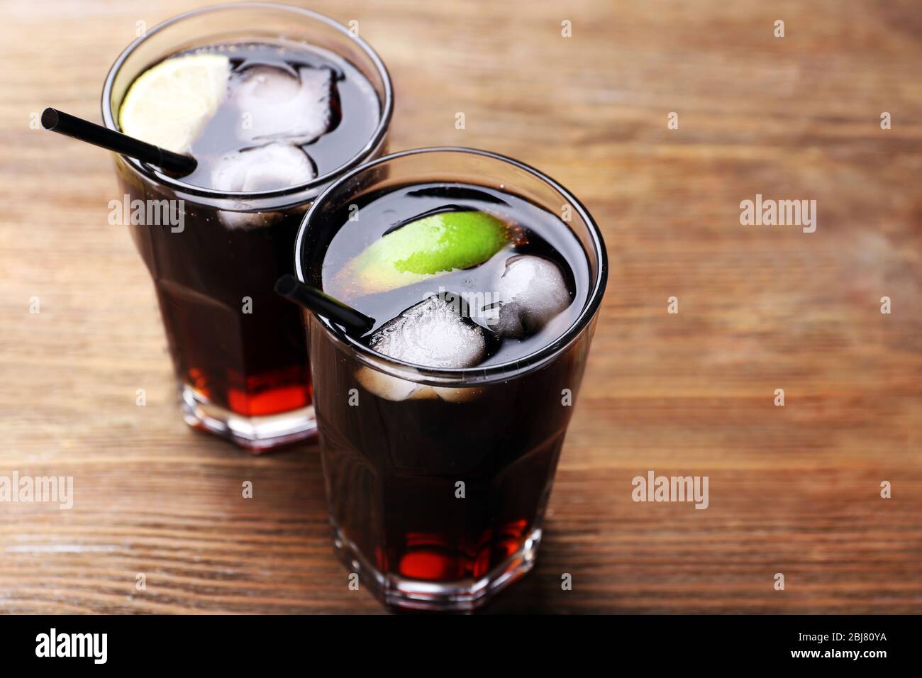 Cocktails with lime slices and ice blocks on wooden table, close up ...