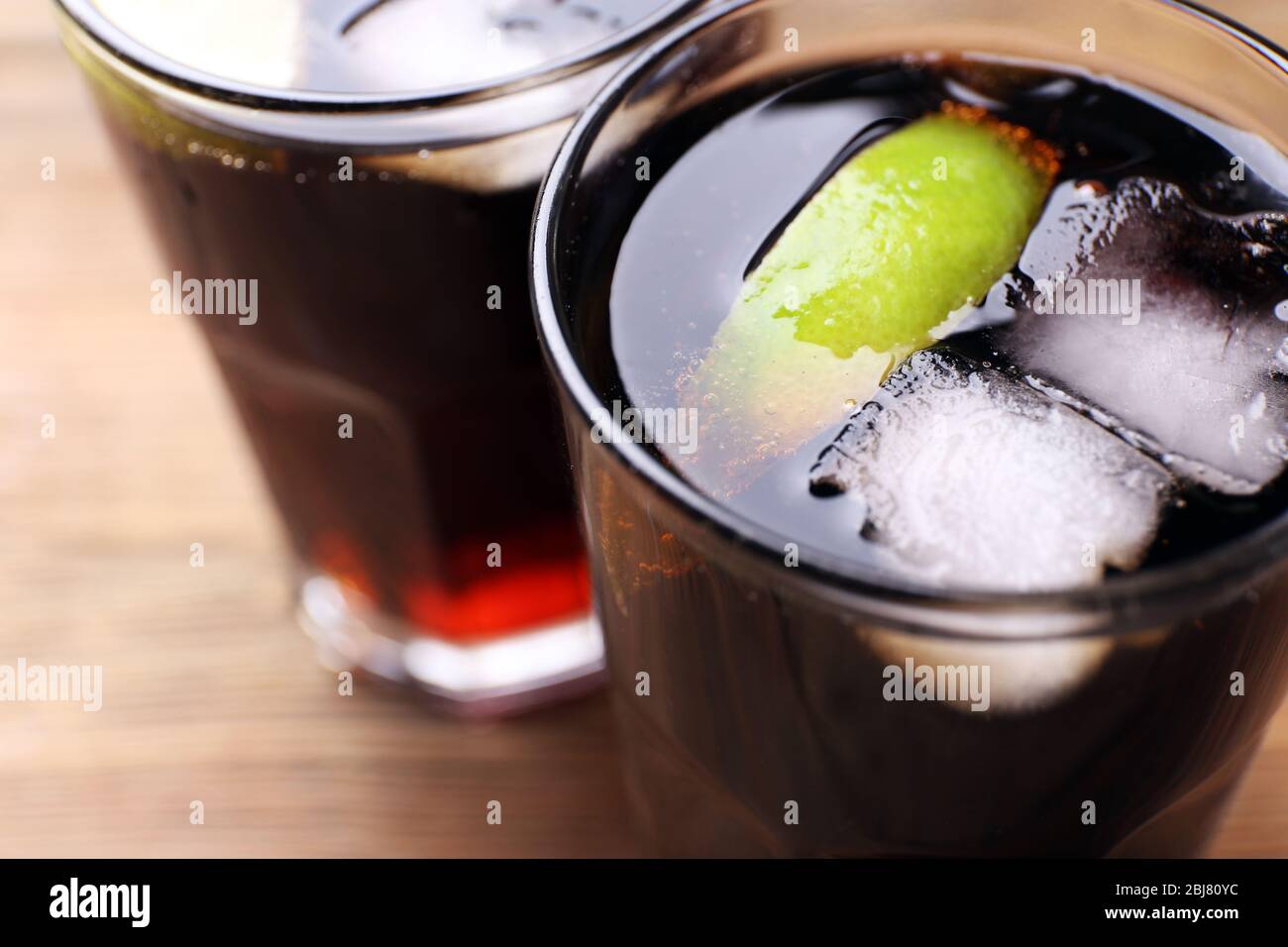 Cocktails with lime slices and ice blocks on wooden table, close up ...