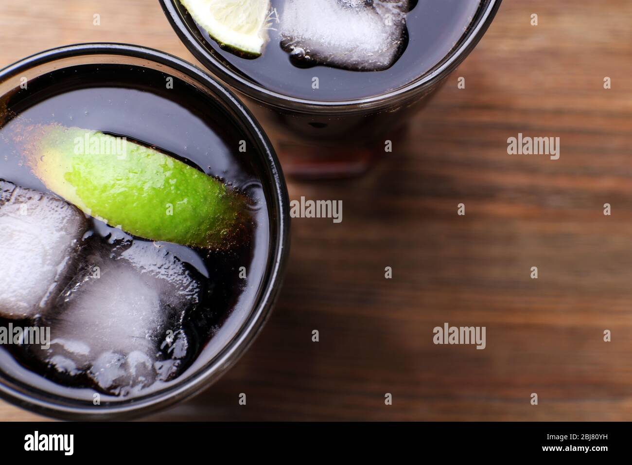 Cocktails with lime slices and ice blocks on wooden table, close up ...