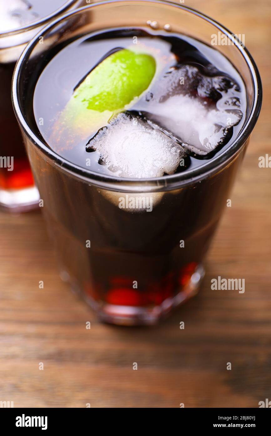 Cocktails with lime slices and ice blocks on wooden table, close up ...