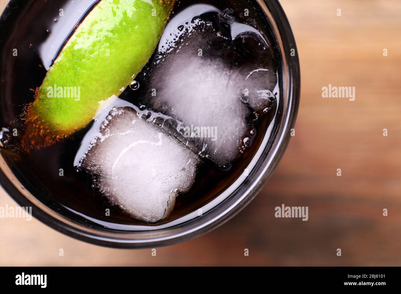 Cocktail with lime slices and ice blocks on wooden table, close up ...