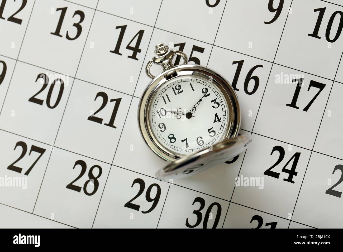 Vintage silver pocket watch laying on calender page with dates, top ...