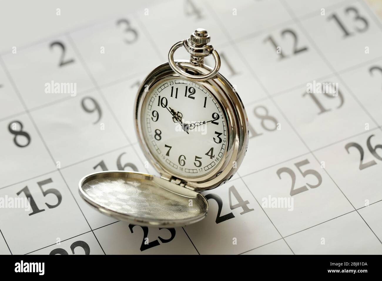 Vintage silver pocket watch laying on calender page with dates, close ...
