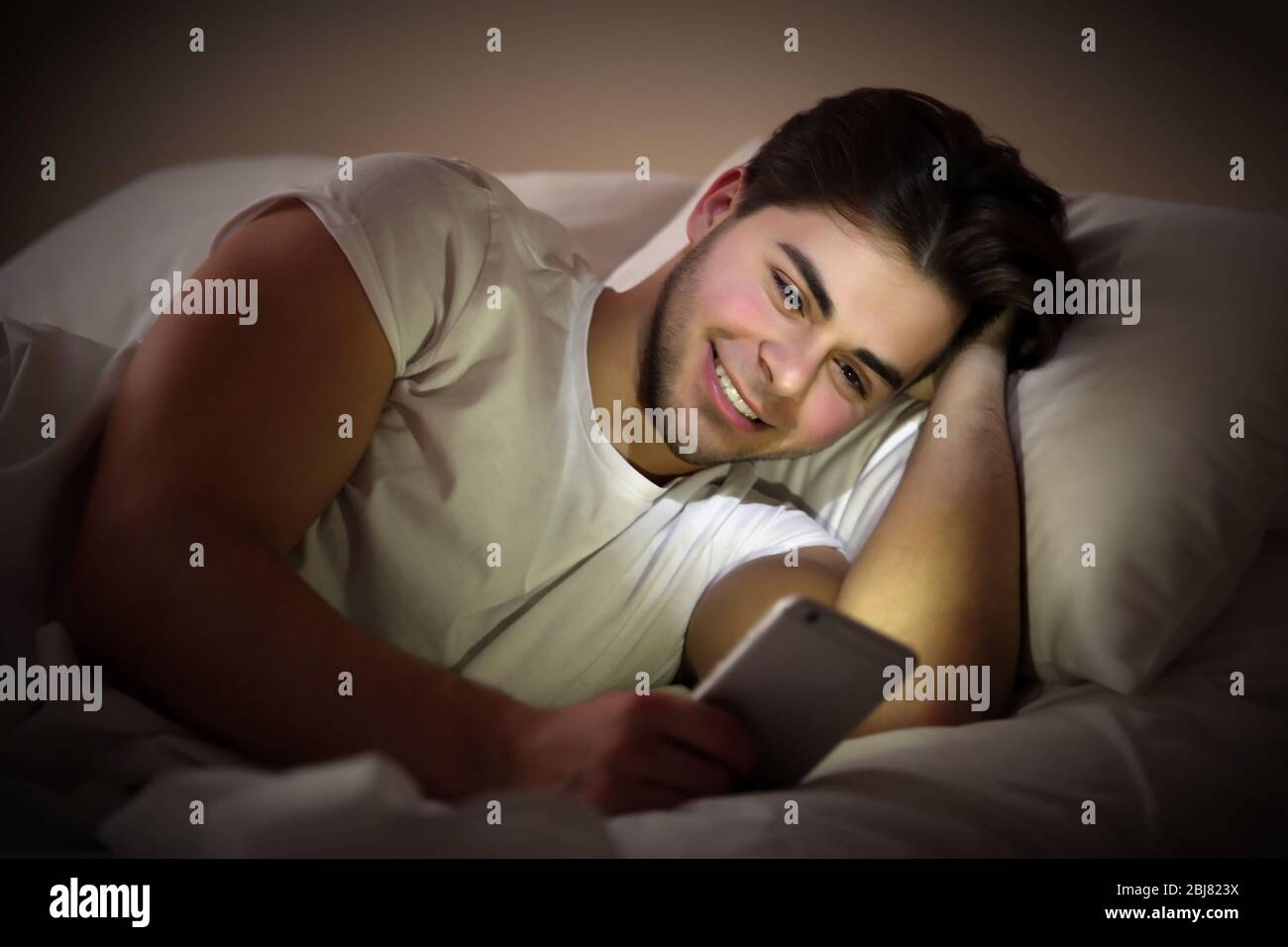 Young man lying on bed with mobile phone in bedroom Stock Photo - Alamy