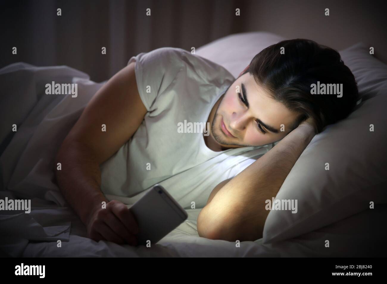 Young man lying on bed with mobile phone in bedroom Stock Photo - Alamy