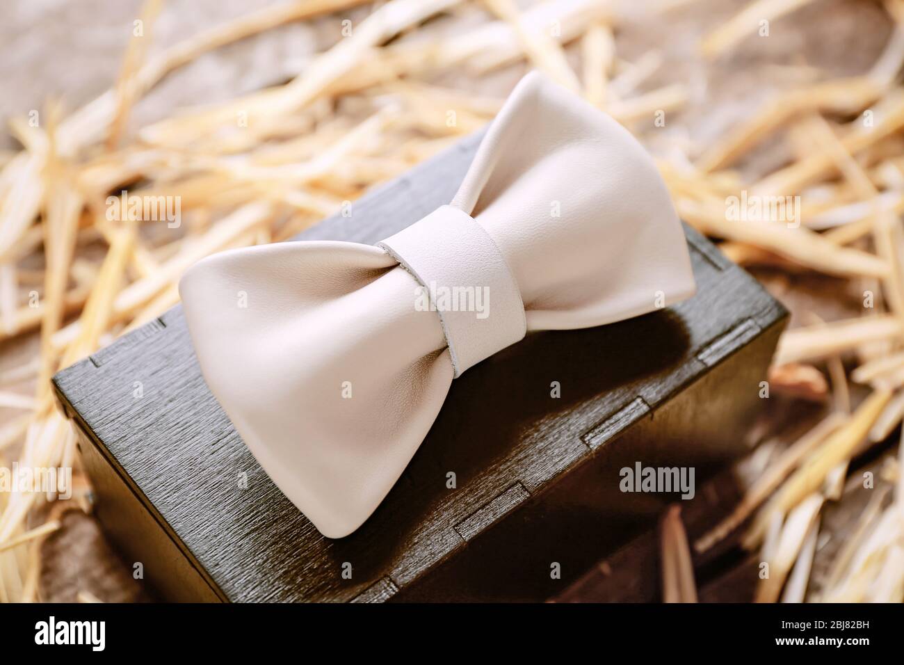 White leather bow tie with special packaging on a thatch, close up ...