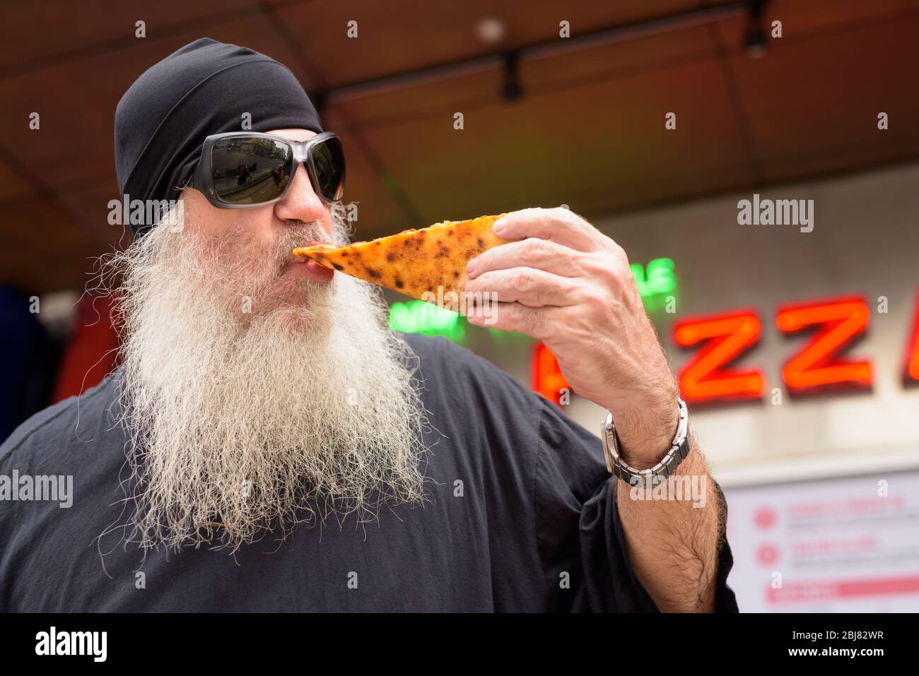 Mature bearded man eating New York style pepperoni pizza outdoors Stock ...