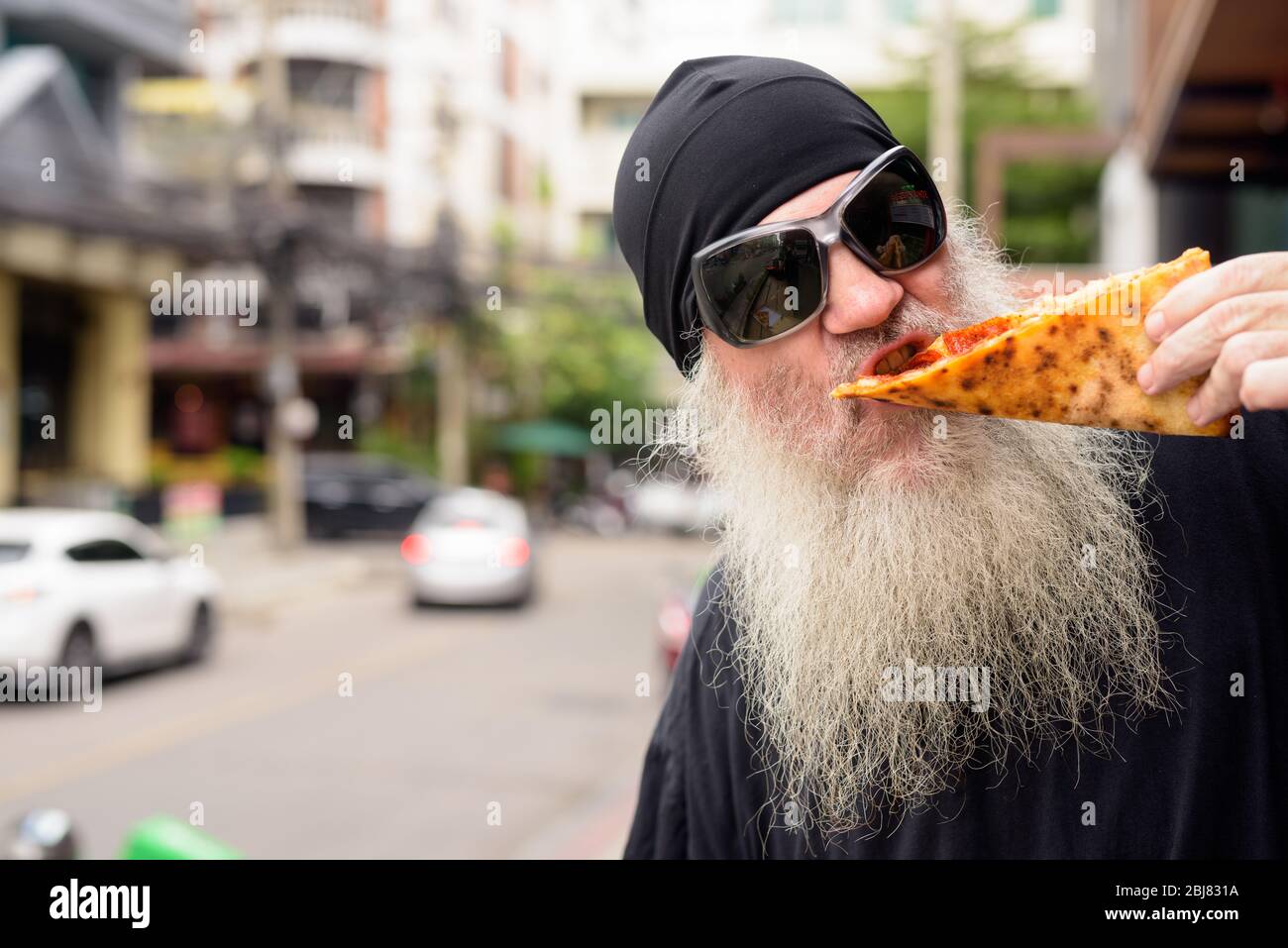 Mature bearded man eating New York style pepperoni pizza outdoors Stock ...