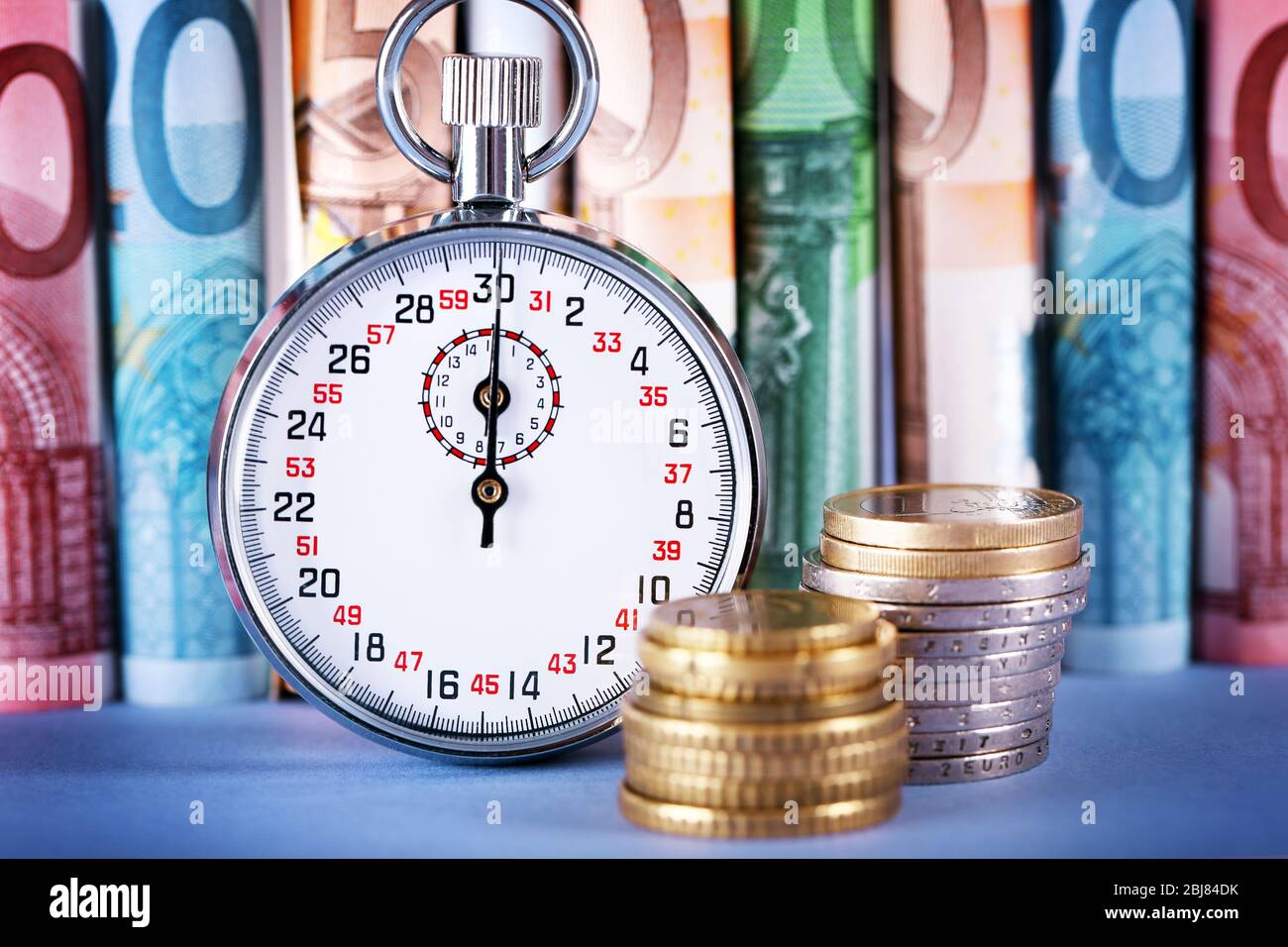 Stopwatch with twisted euro banknotes and coins on blue background ...