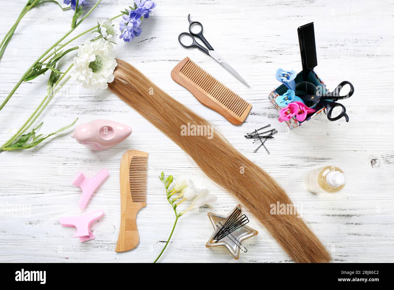 Strand of hair with flowers and barber tools on light wooden background ...