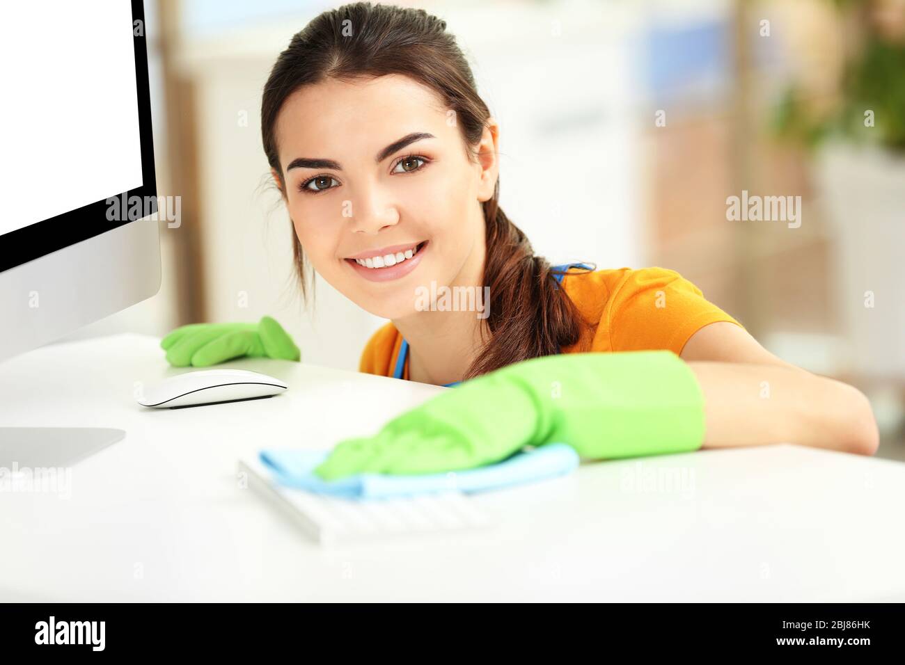 Young woman cleaning workplace with computer monitor in the office ...