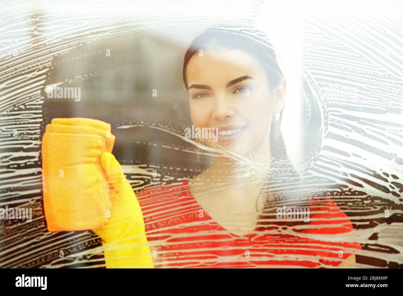 Young woman washing window glass with duster inside Stock Photo - Alamy