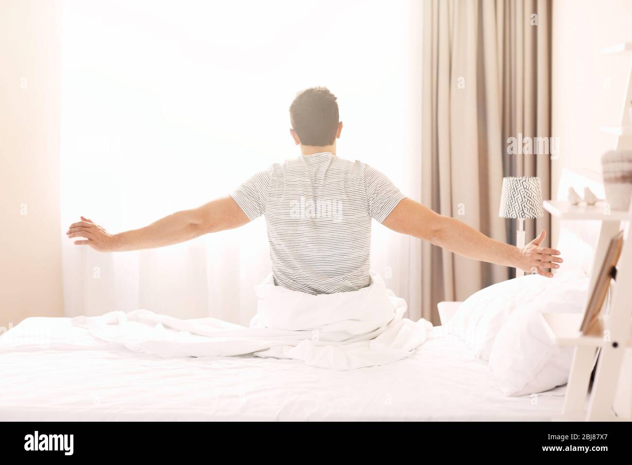 A young man waking up in bed and stretching his arms Stock Photo - Alamy