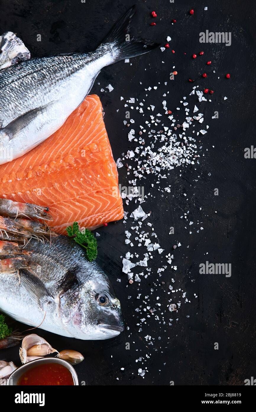 Fresh raw fish and seafood on black background. Top view with copy ...