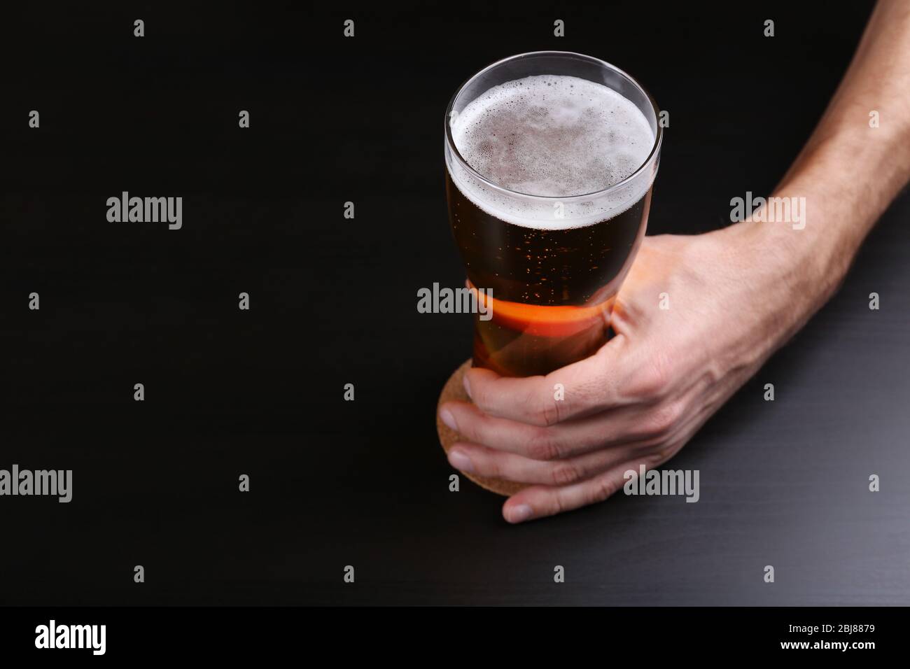 Male hand holding glass of beer on dark background Stock Photo - Alamy