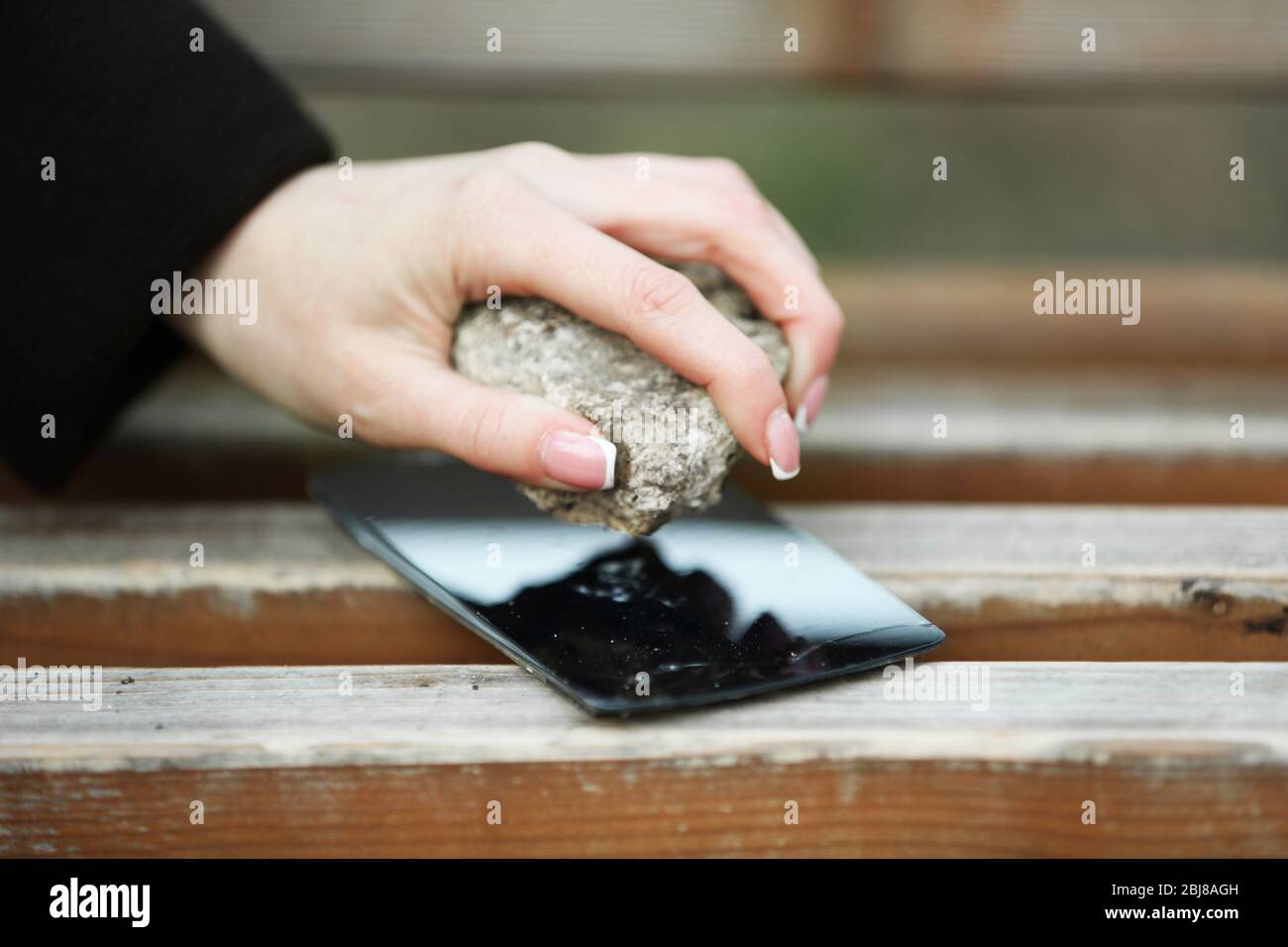 Female hand crushing with stone screen of mobile phone on wooden bench ...