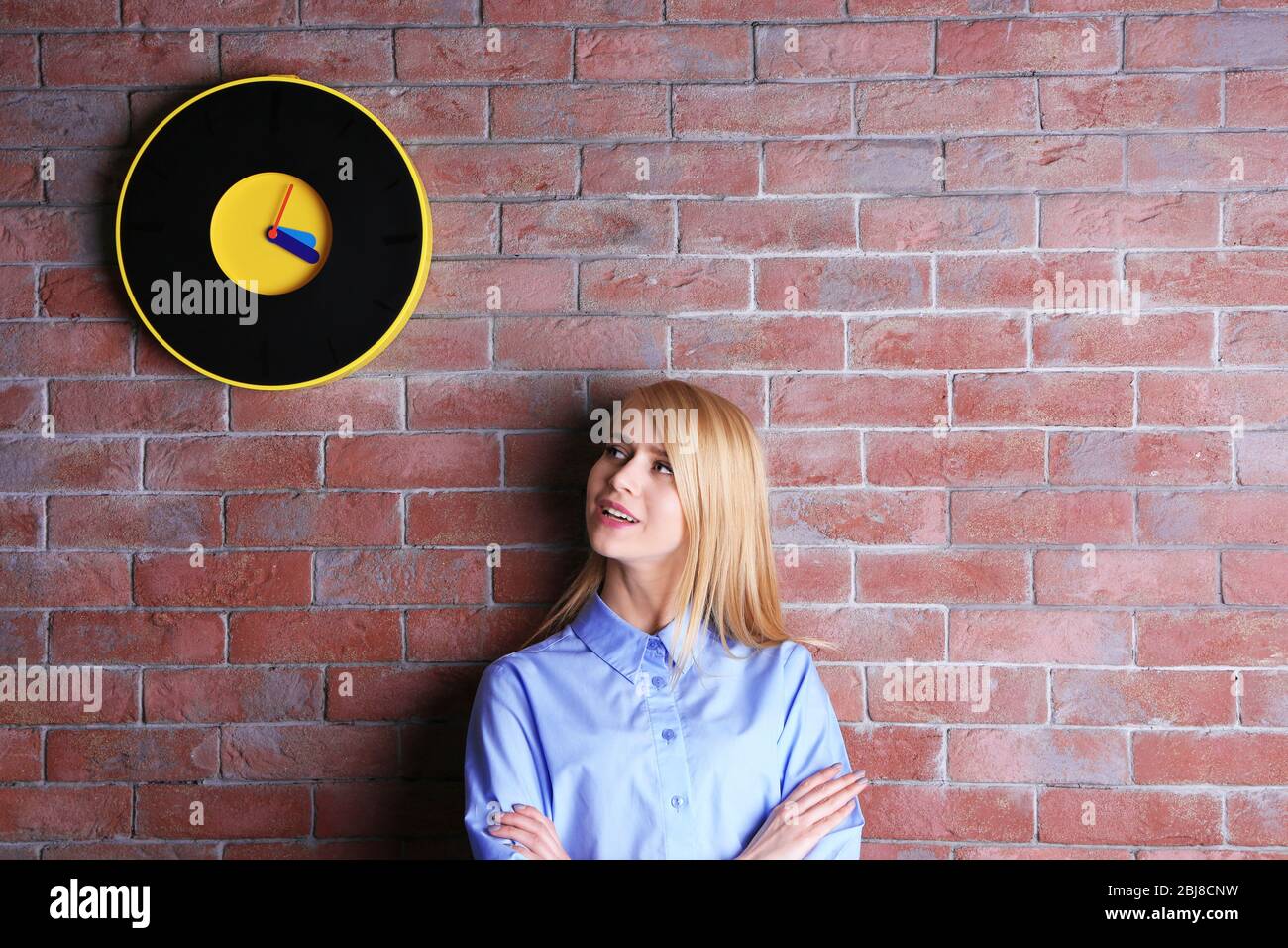 Young attractive woman under the clock, on brick wall background Stock ...