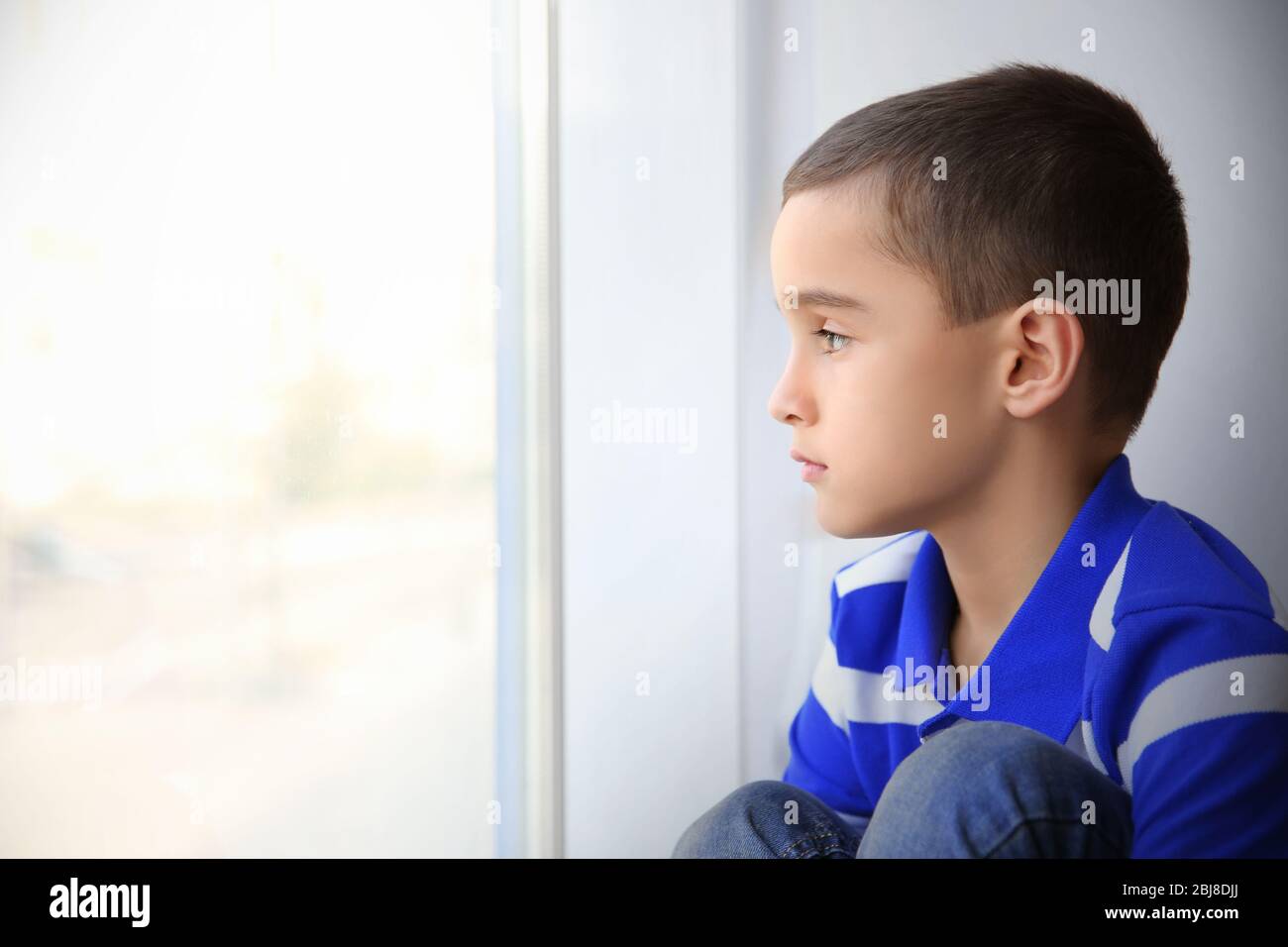 Single boy sitting on windowsill indoors Stock Photo - Alamy
