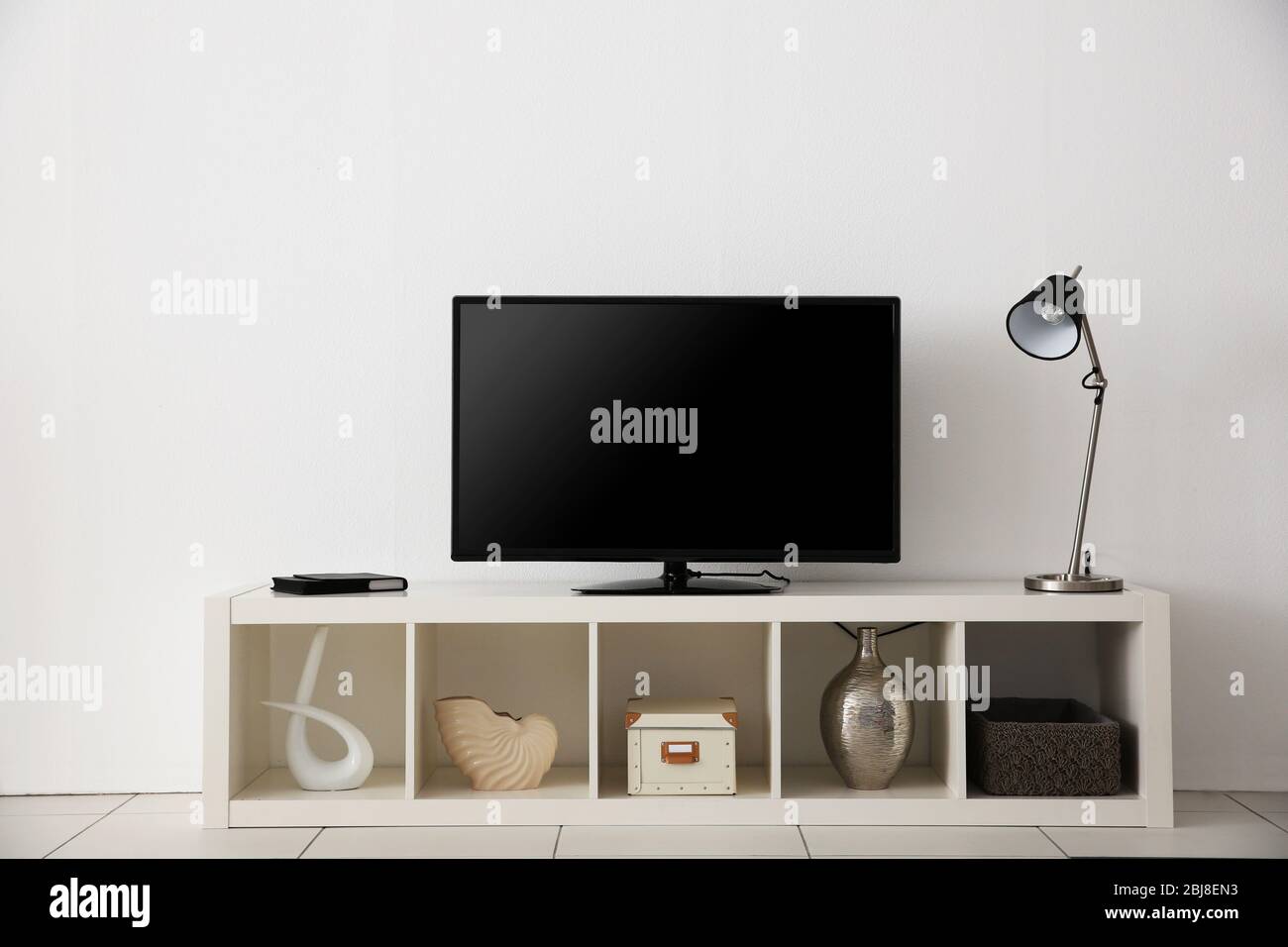 wide screen TV on white stand near light wall Stock Photo - Alamy