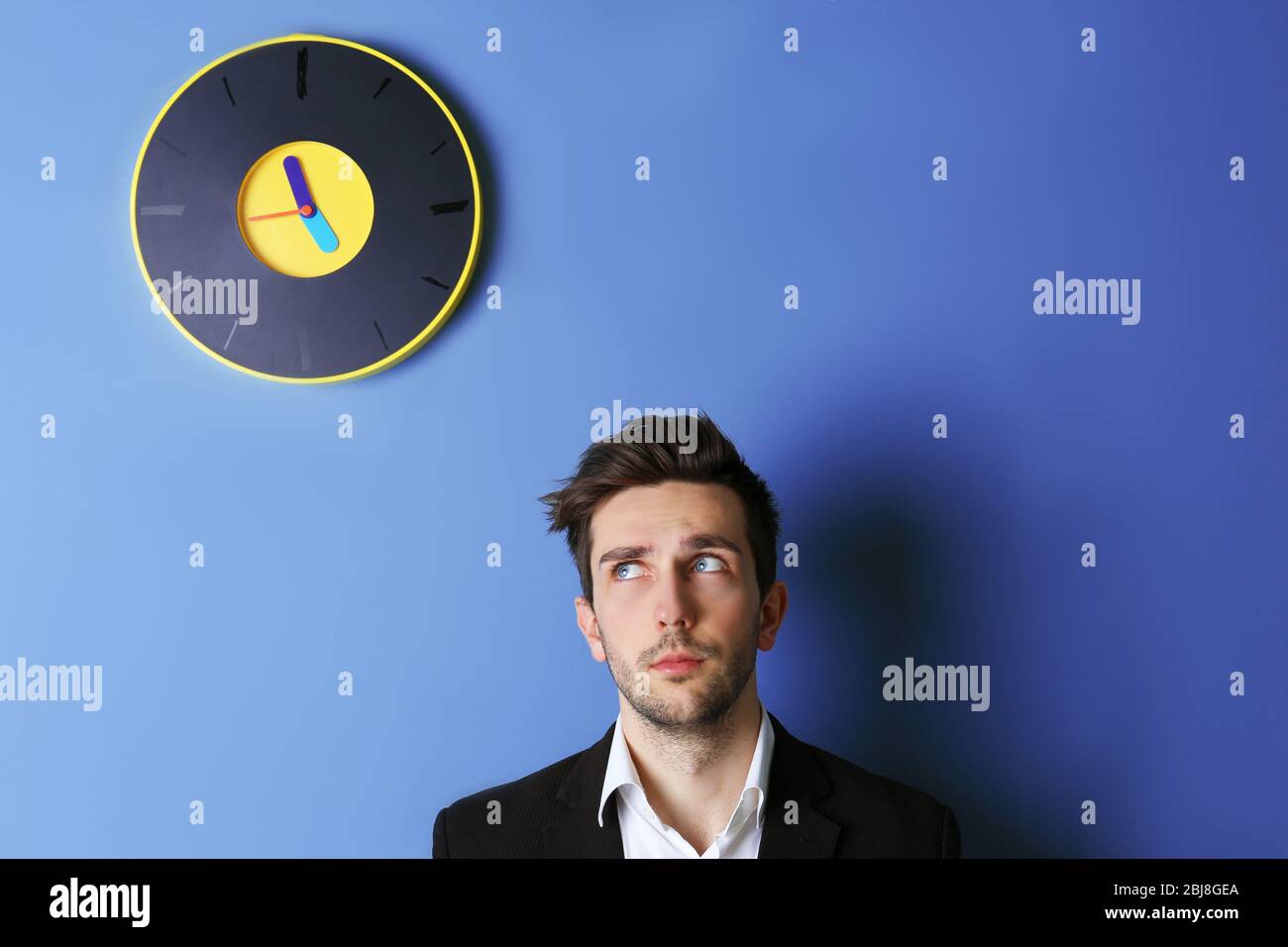 Man in black suit standing beside a big clock on blue wall Stock Photo ...