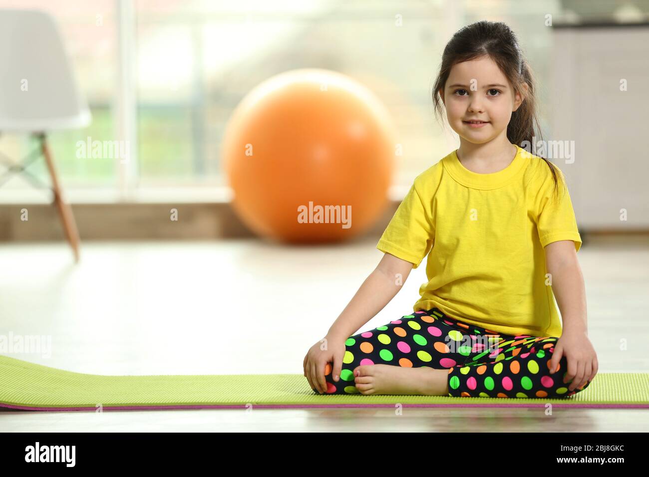 Little cute girl sitting on a mat indoor Stock Photo - Alamy