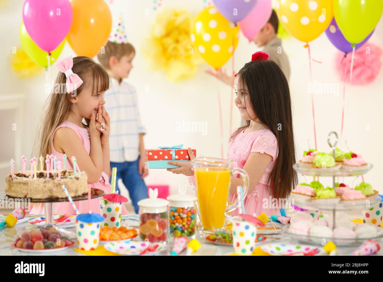 Happy little girl presenting a gift to her friend at birthday party ...