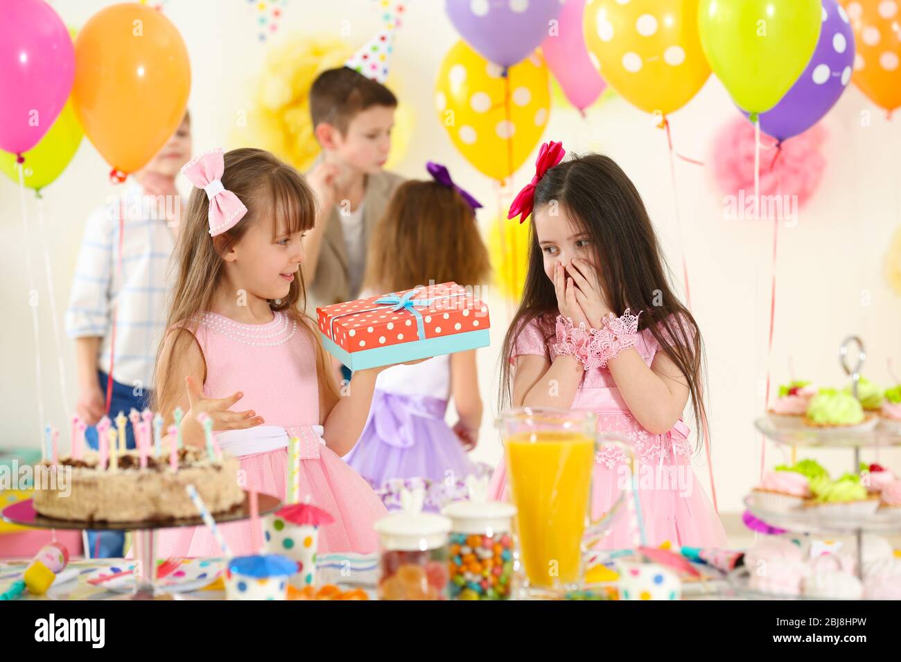 Happy little girl presenting a gift to her friend at birthday party ...