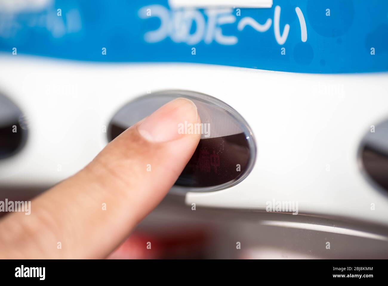 A finger pressing a button on a Japanese vending machine to buy a drink ...