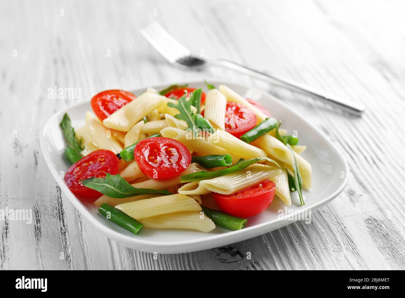 Boiled penne pasta with tomatoes, French bean and arugula on white ...