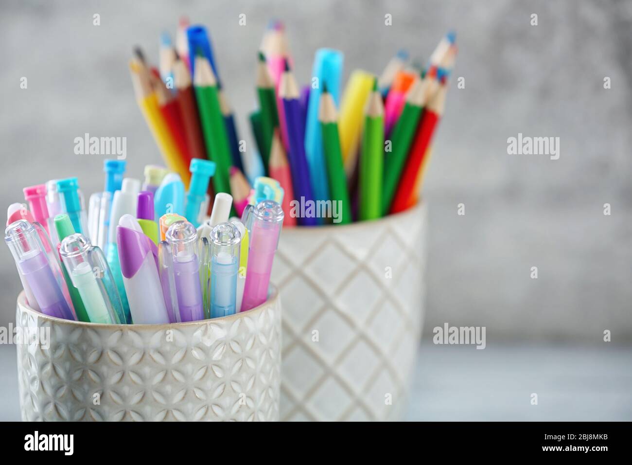 Pens and pencils in cups in front of wall background Stock Photo - Alamy
