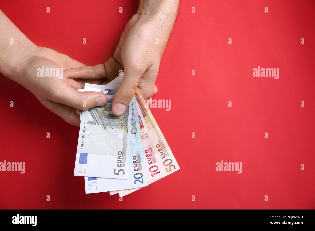 Male hands counting euro banknotes on red background Stock Photo - Alamy