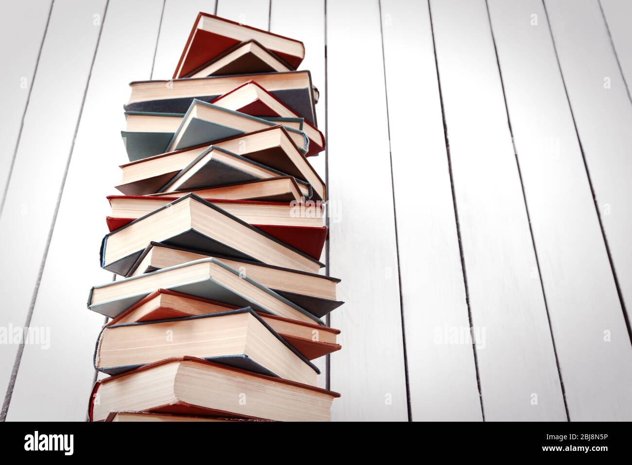High stack of books on white wooden wall background Stock Photo - Alamy