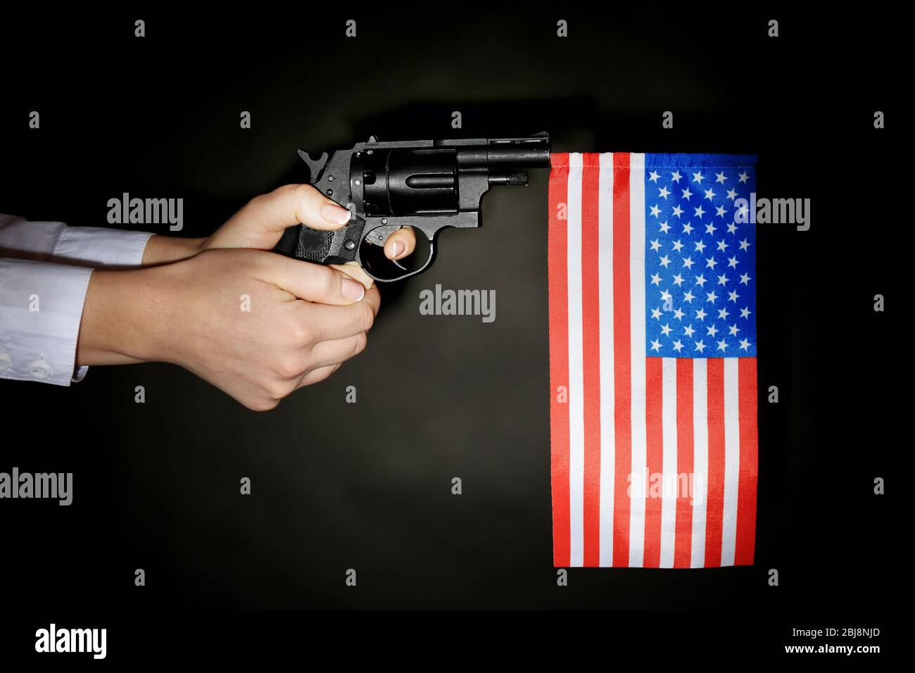 Woman holding handgun with inserted USA national flag on dark lighted ...