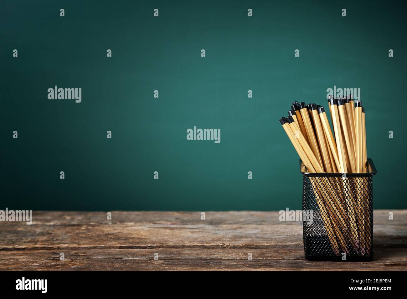 Many pencils in the metal holder on wooden table on green board ...