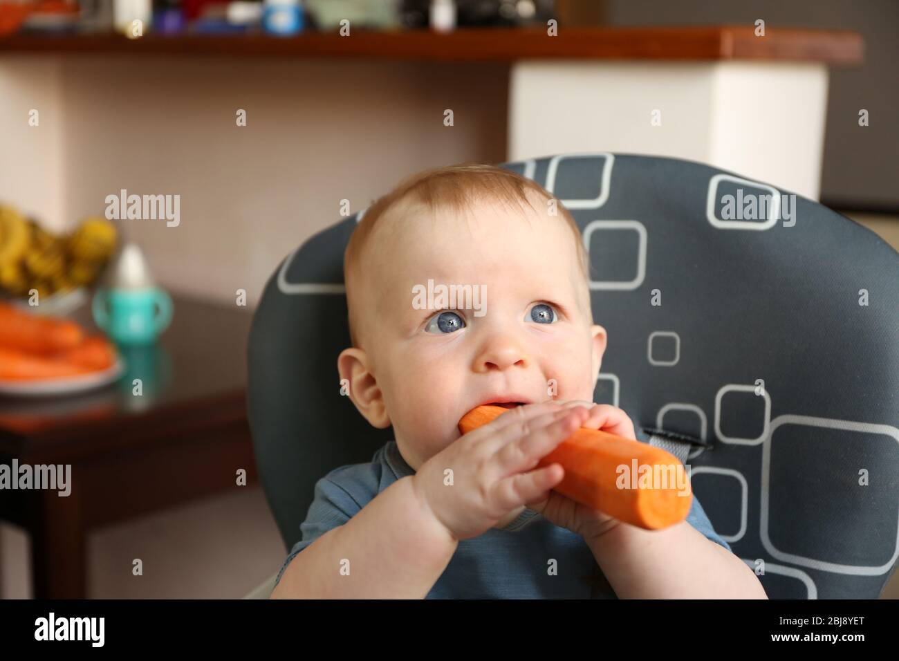 Baby eating carrot in a chair Stock Photo - Alamy