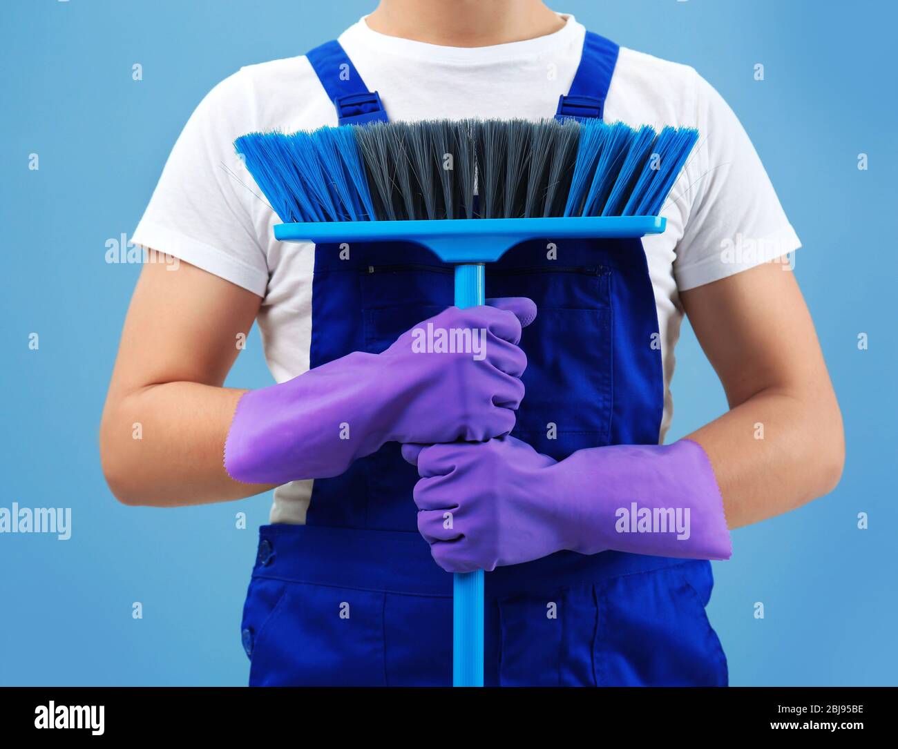 Man holding broom on grey background Stock Photo - Alamy