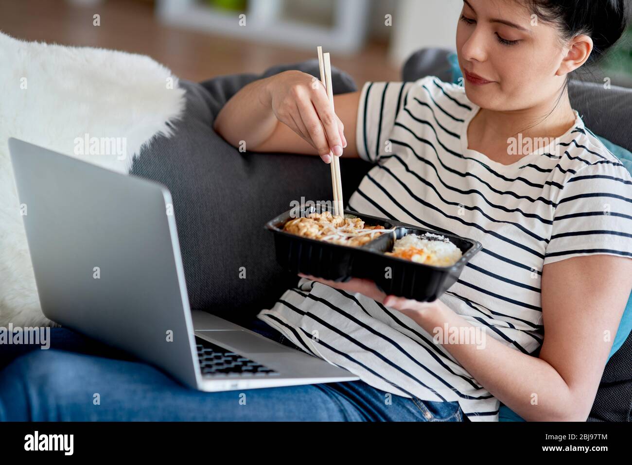 Young Asian woman eating while watching something on a laptop Stock ...