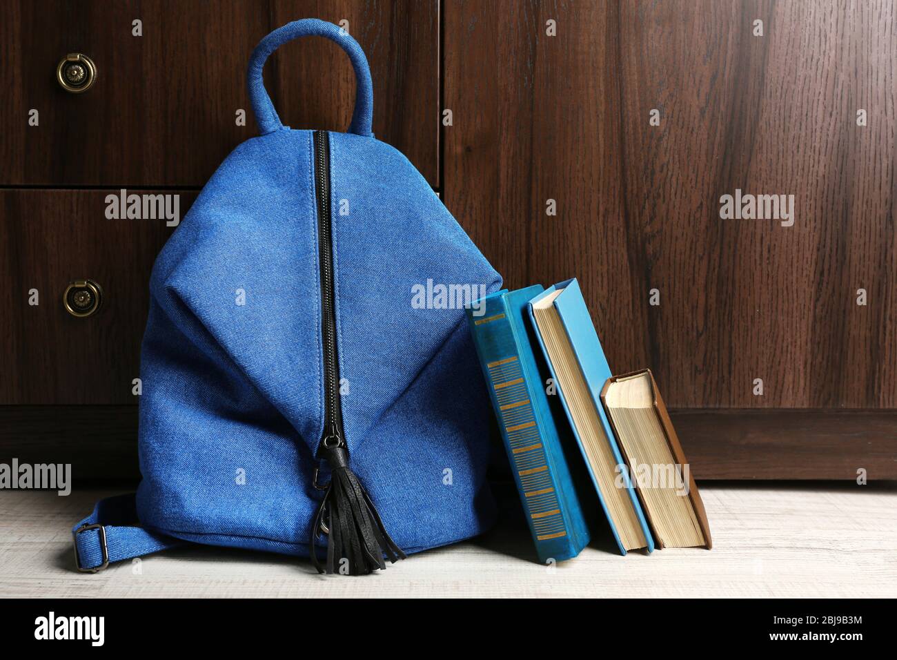 Blue jeans backpack with books on brown background Stock Photo - Alamy