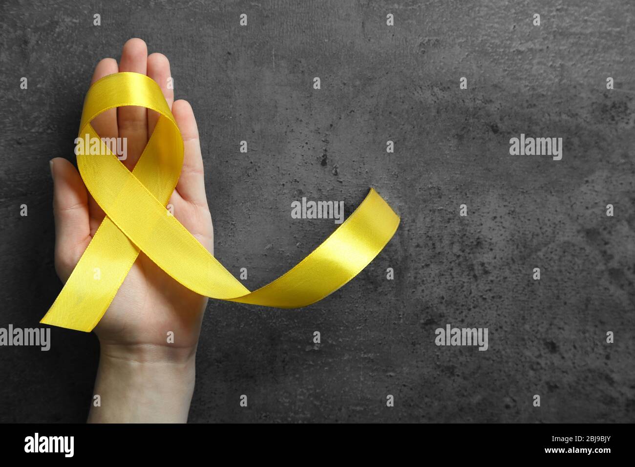 Hand holding yellow ribbon on dark background Stock Photo - Alamy