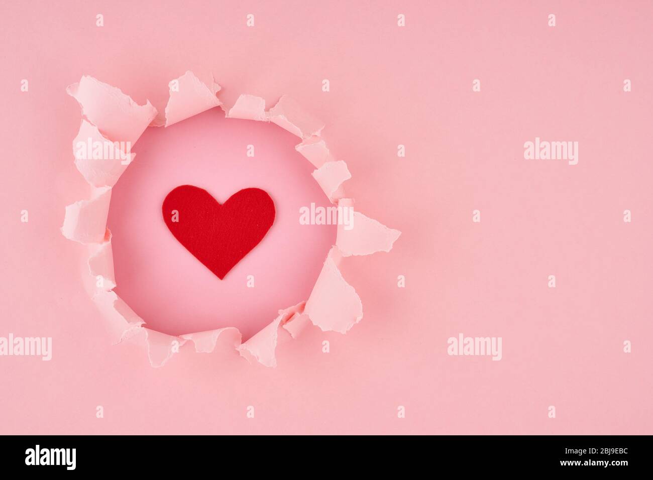Valentine's Day. A ripped hole and red heart in bright pink textured ...