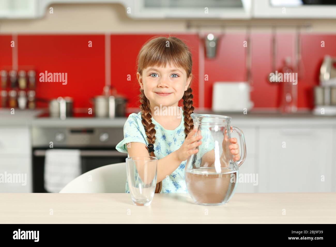 Cute little girl with jug of water in kitchen Stock Photo - Alamy