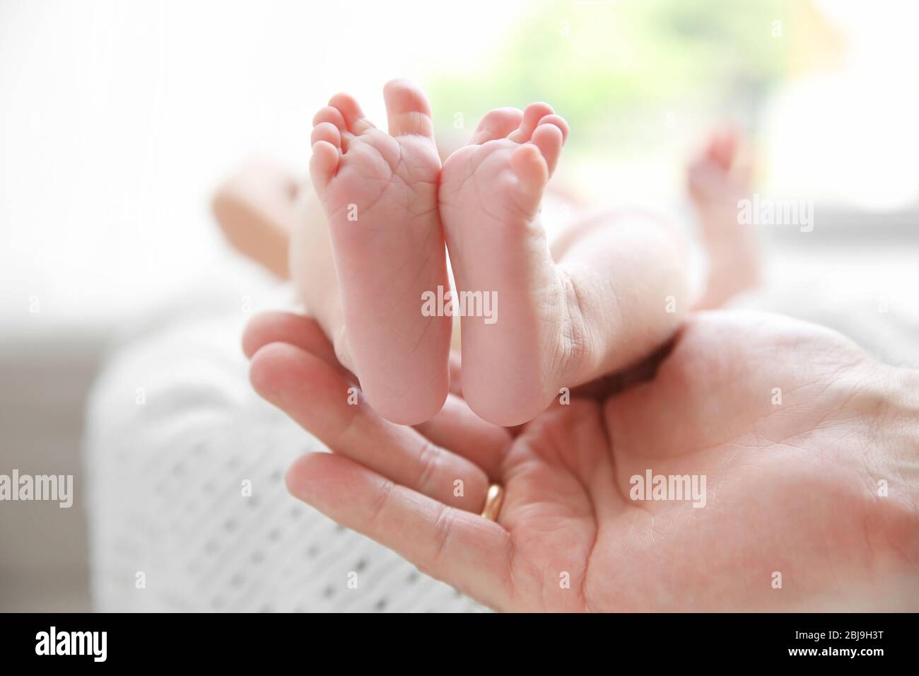 Female hand holding feet of newborn baby girl lying on soft blanket ...