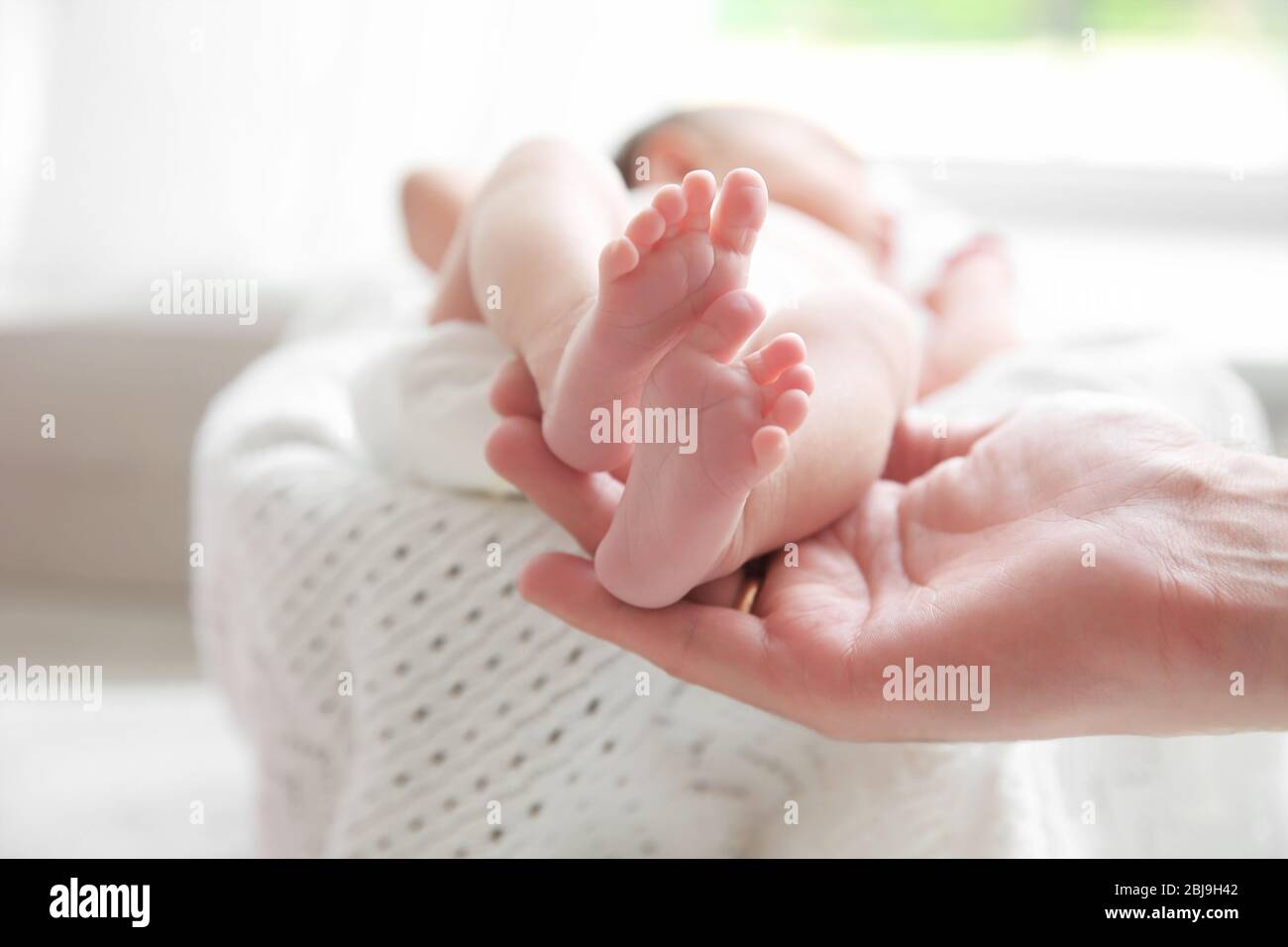Female hand holding feet of newborn baby girl lying on soft blanket ...