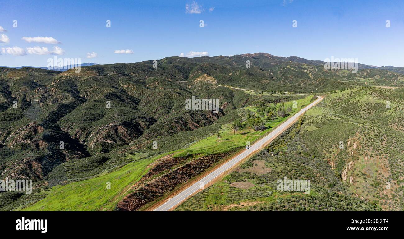 Long empty two lane road leads through a vast open green wooded ...
