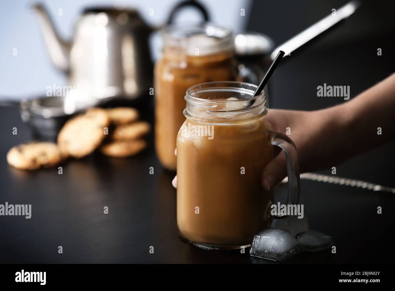 Female hand holding iced coffee in glass jar on black table Stock Photo ...